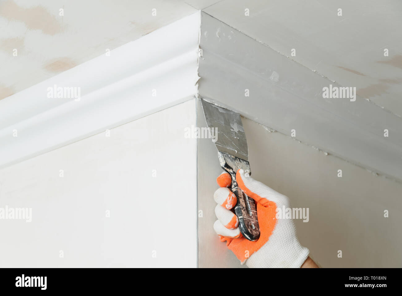 Installation of ceiling moldings. Worker puts glue on plastic molding ...