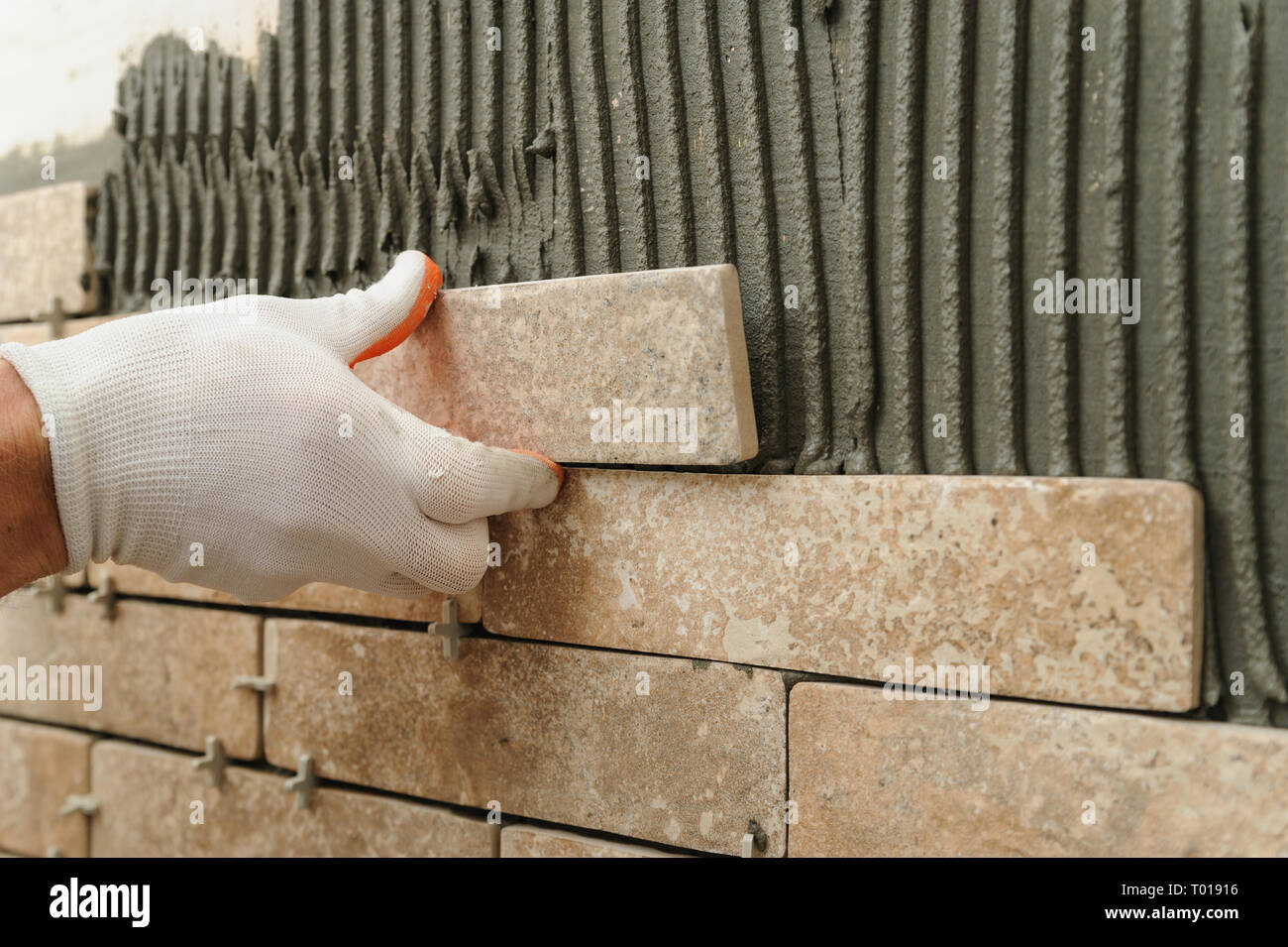 Installing the tiles on the wall. A worker putting tiles in the form of ...