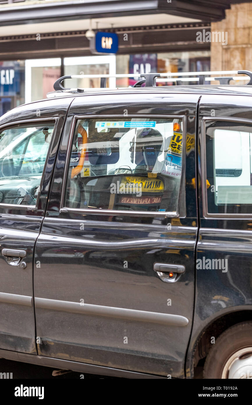 Minicab sign reflected in a black cab window, Kensington High St ...