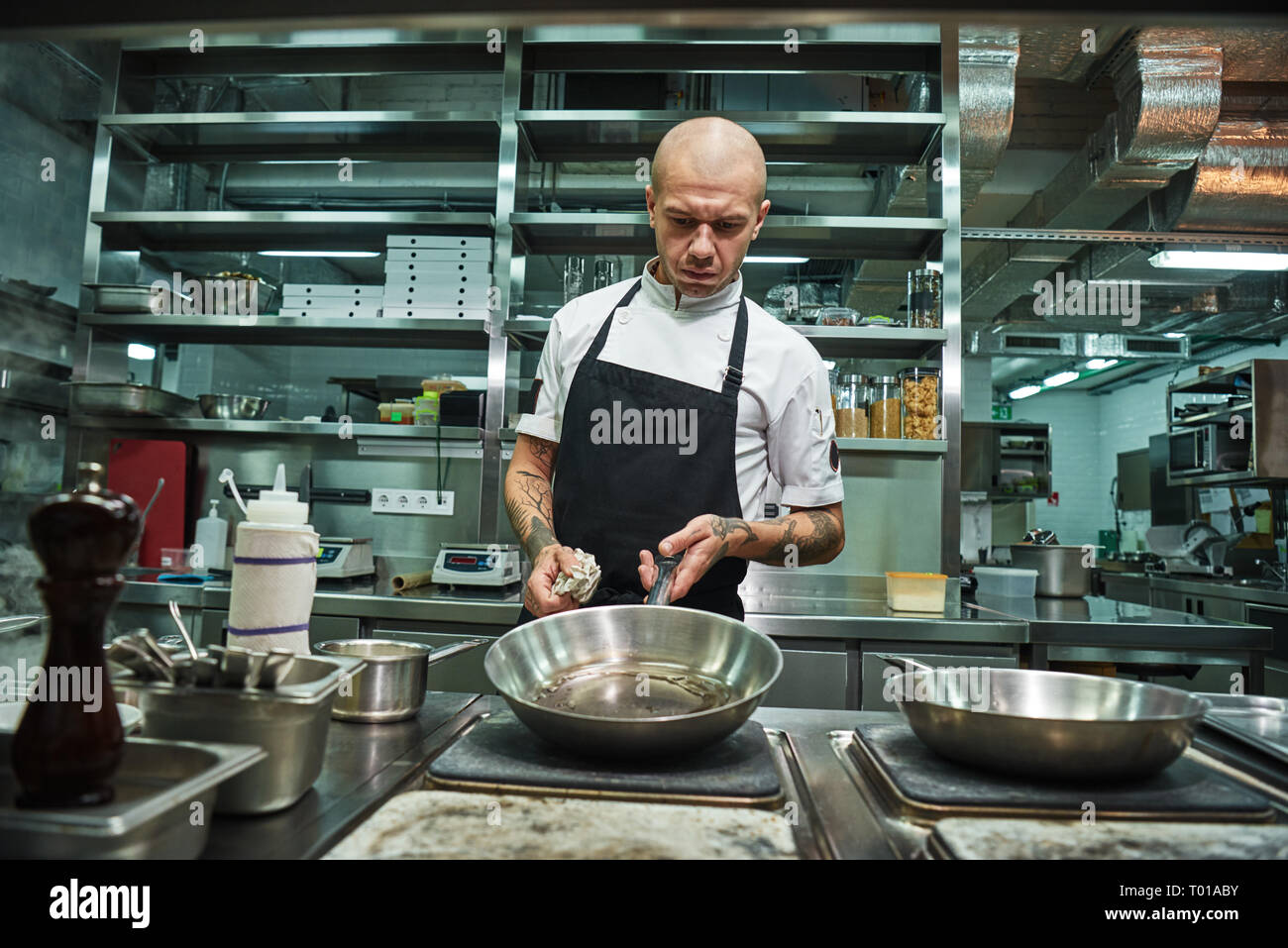 Cooking process. Brutal male chef with several tattoos on his arms ...
