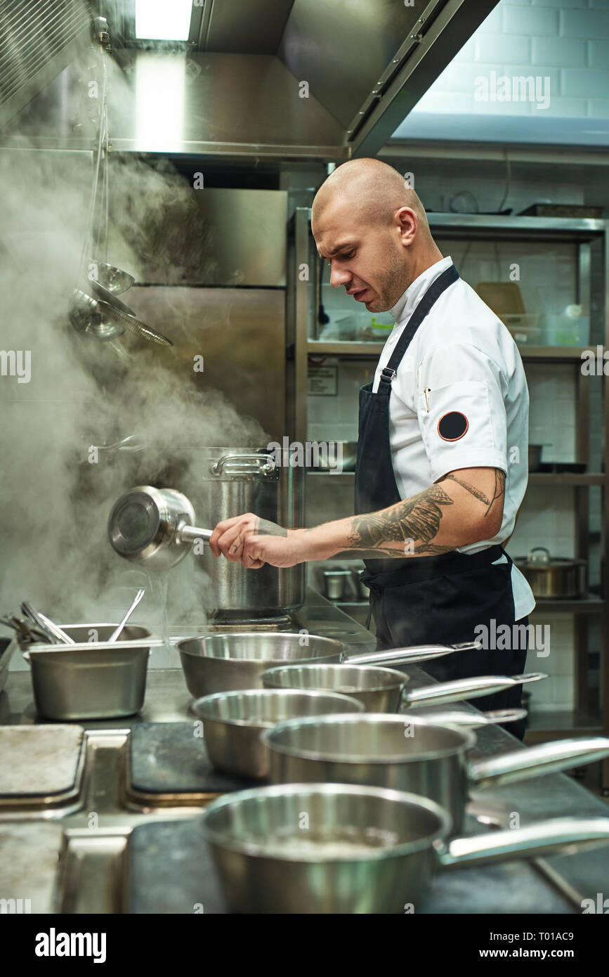 Focused on a process. Side view of handsome and young chef cooking ...