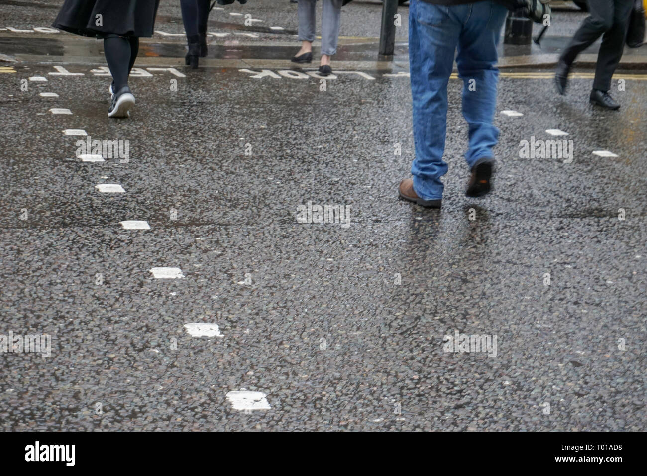 close-up of pedestrians' feet crossing a wet road with dashed lines and ...