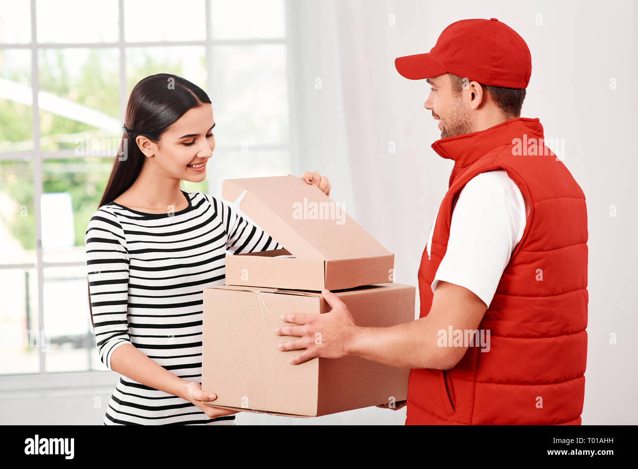 Cheerful postman wearing red postal uniform is delivering parcels to a ...