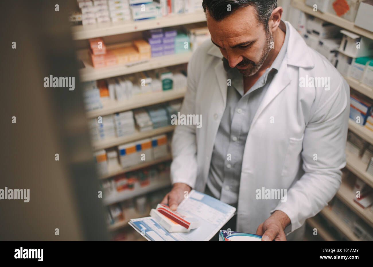Male chemist looking for right medicine with a prescription in pharmacy ...