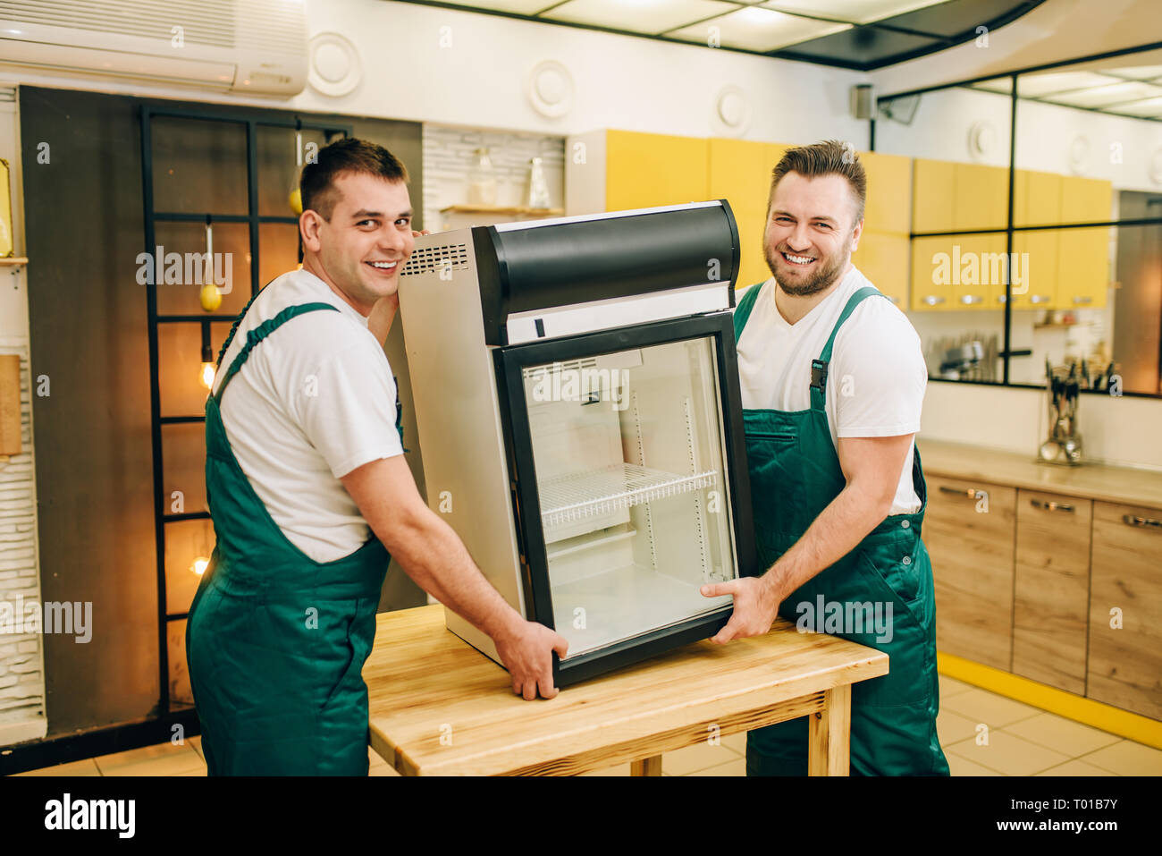 Workers in uniform installs refrigerator at home Stock Photo - Alamy