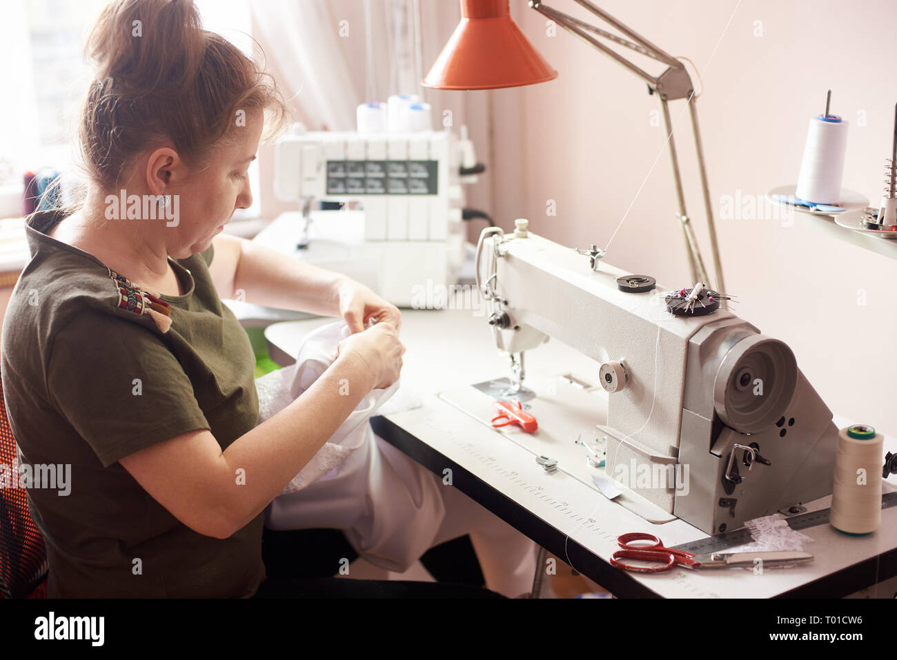 Clothier sitting in atelier, stitching white dress with hands and ...