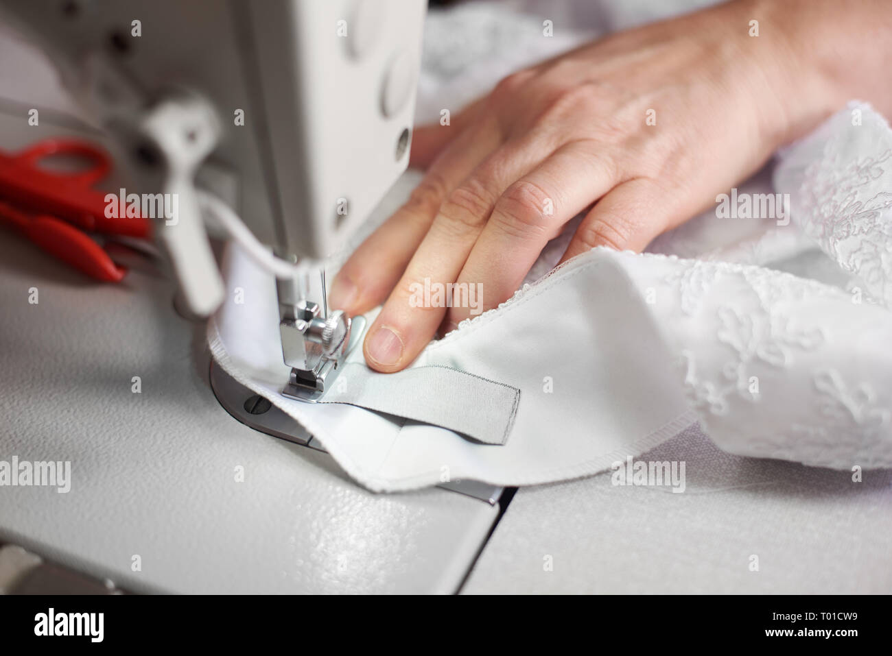 Close up front view of female hands sewing on auxiliary detail to white ...