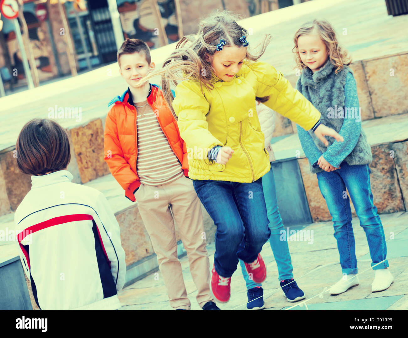 Positive kids playing in jump rope game at city street Stock Photo - Alamy