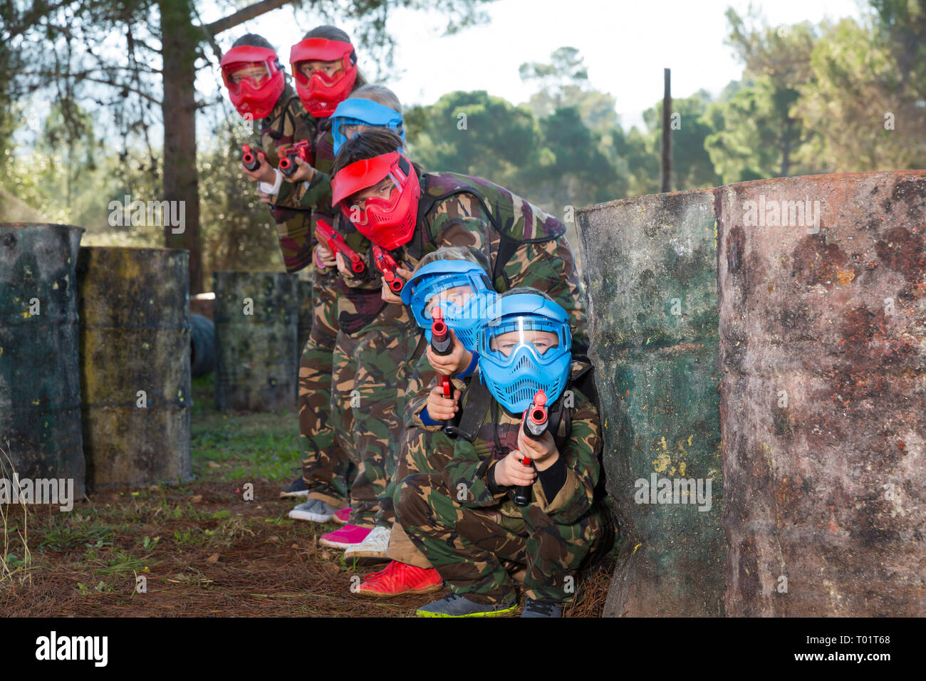 Group of happy kids in camouflages and masks playing paintball aiming ...