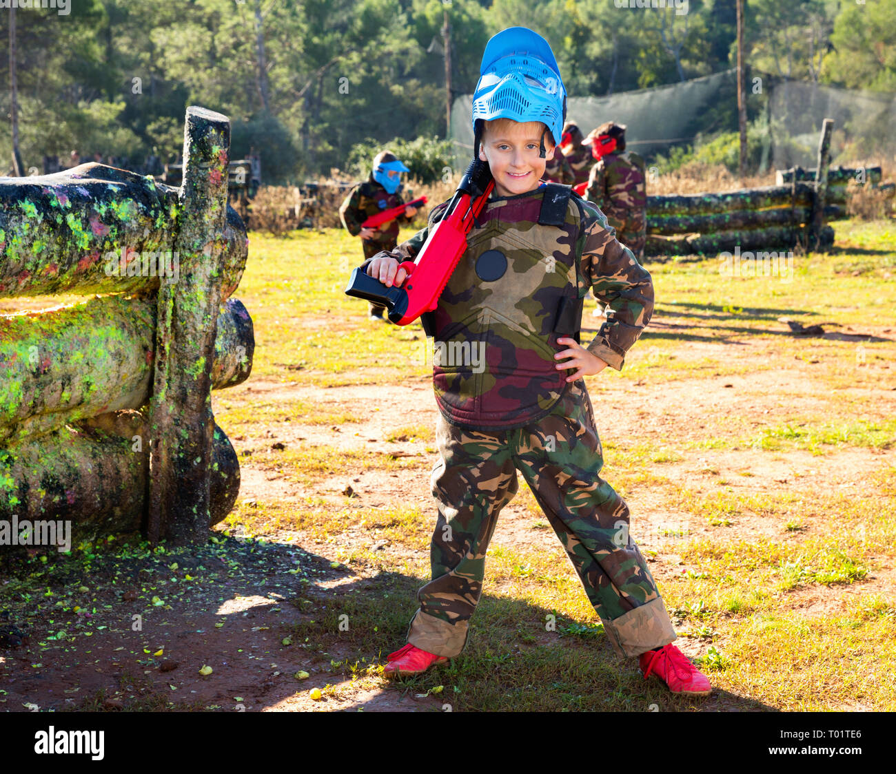 Happy positive boy paintball player in camouflage standing with gun ...
