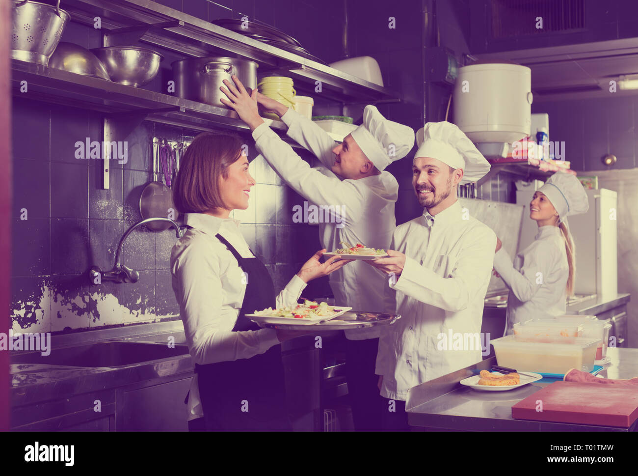 Young woman professional waiter collecting freshly prepared dishes from ...