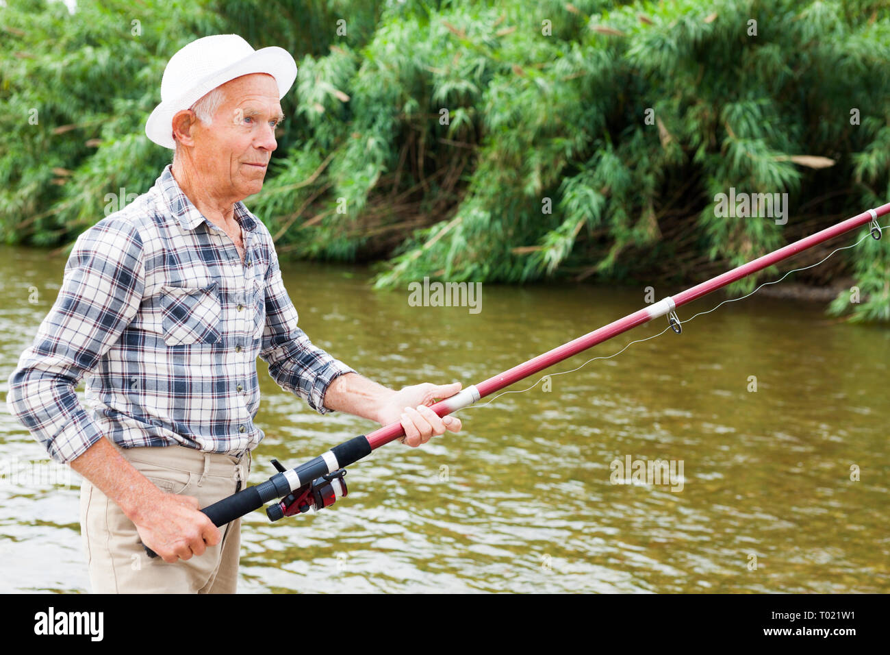 Positive adult man with rod relaxing and enjoying fishing by lakeside ...