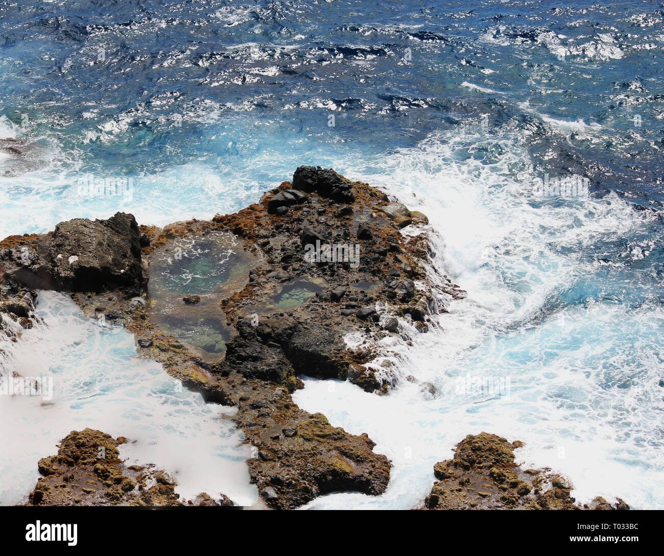 Huge waves splashing around rocks and sharp corals at a tropical beach ...