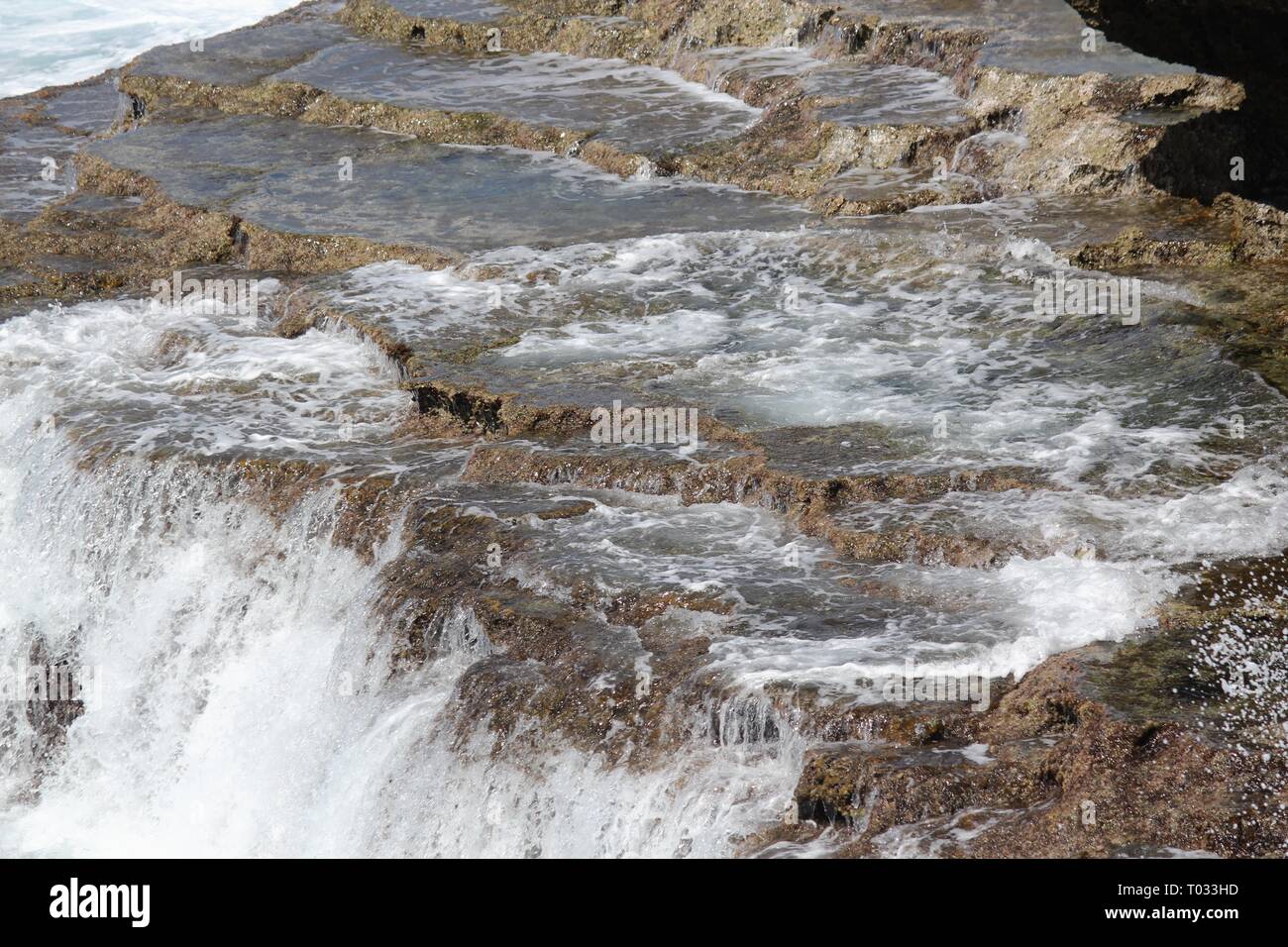Cascades of foaming waters over sharp corals and rock platforms in the ...