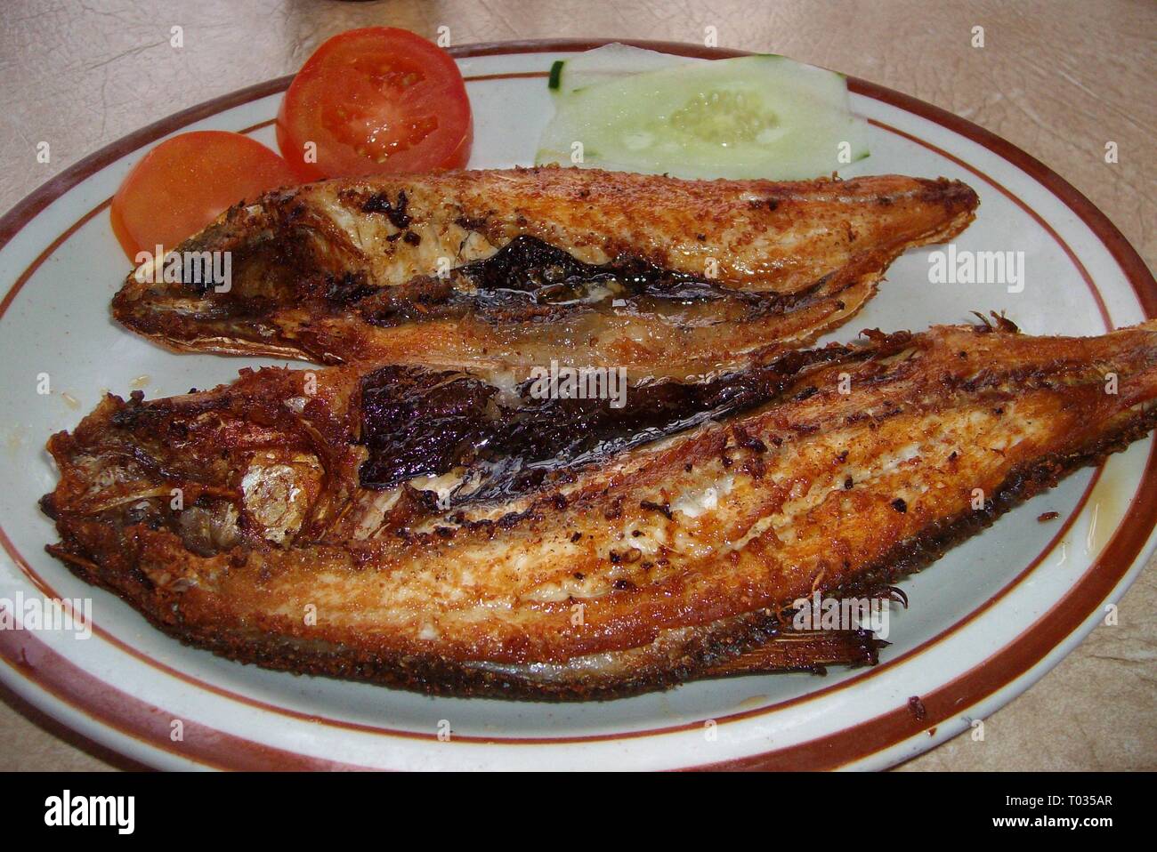 Crispy fried milk fish or bangus served with cucumbers and tomatoes in ...