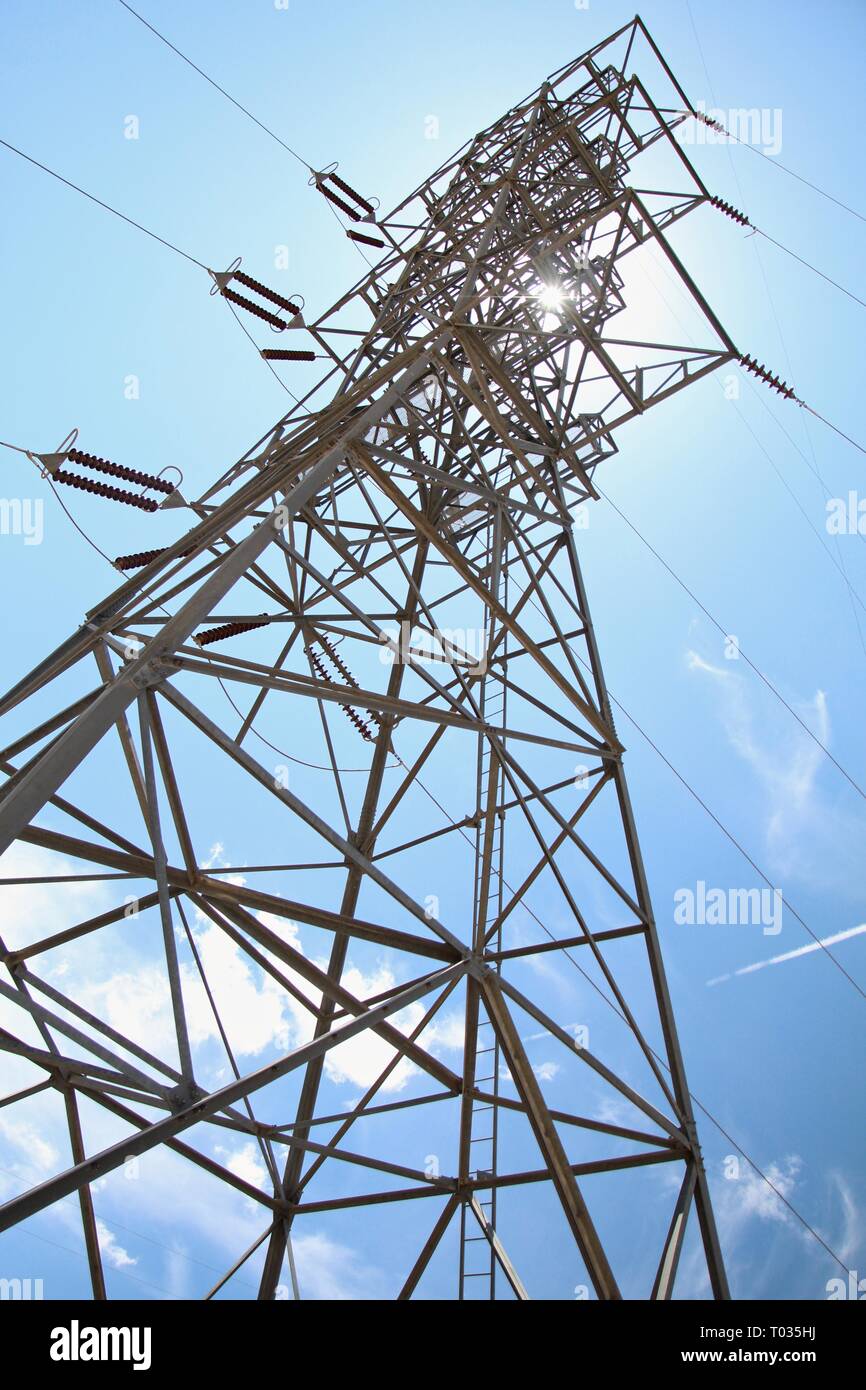 A high voltage power line with the streak of the sun peeking through on ...