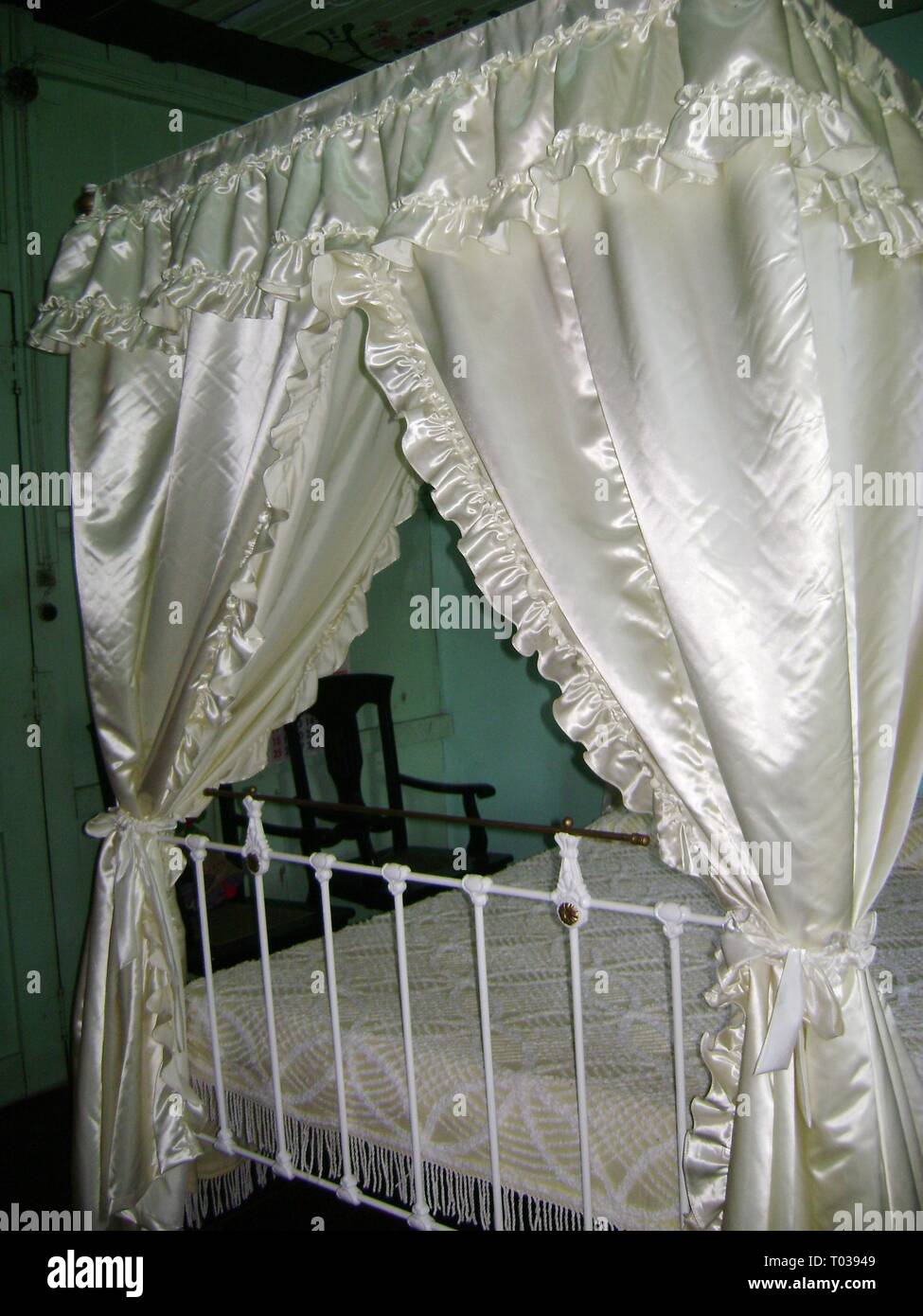 White satin curtain with ruffles covering an antique bed in an old ...