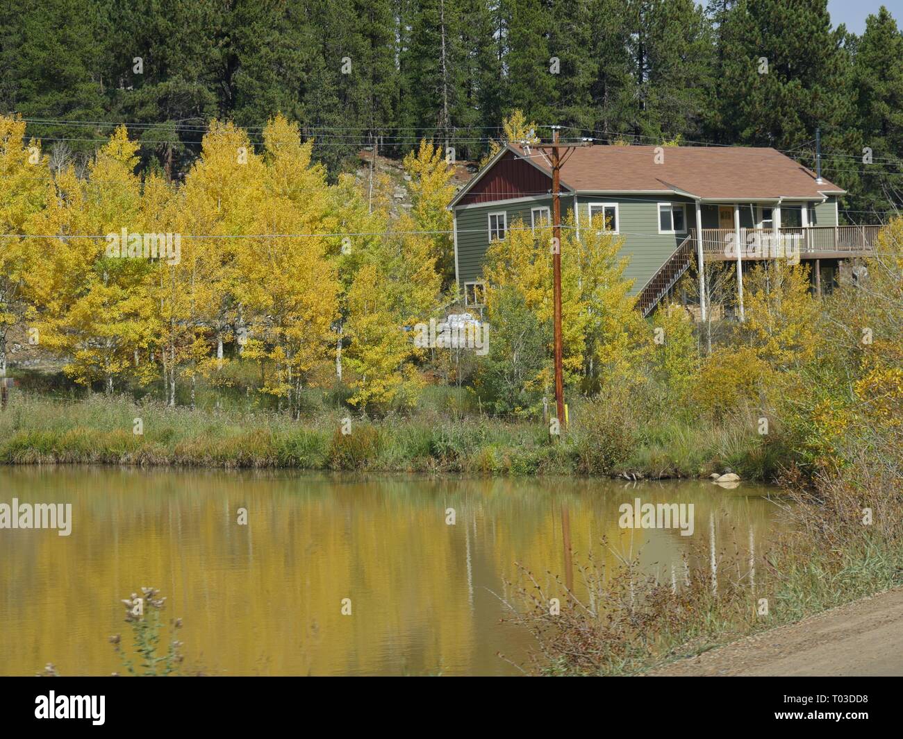 Fall colors reflected in a pond by the roadside, with a cabin in the ...