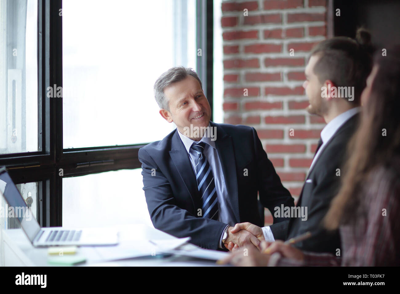 friendly handshake of business partners sitting at a Desk Stock Photo ...