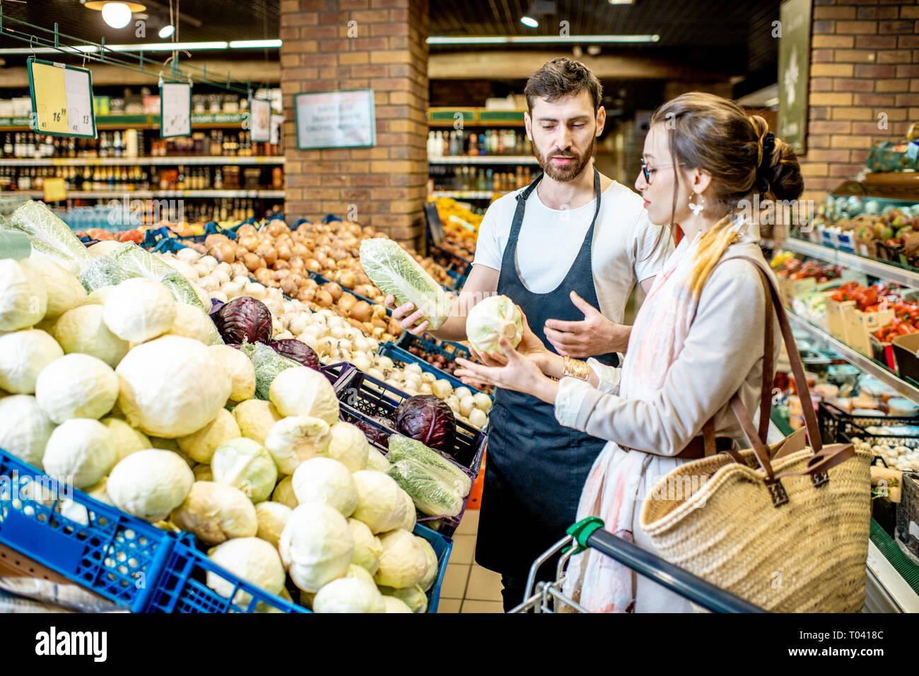 Shop worker helping young woman client to chooose vegetables in the ...