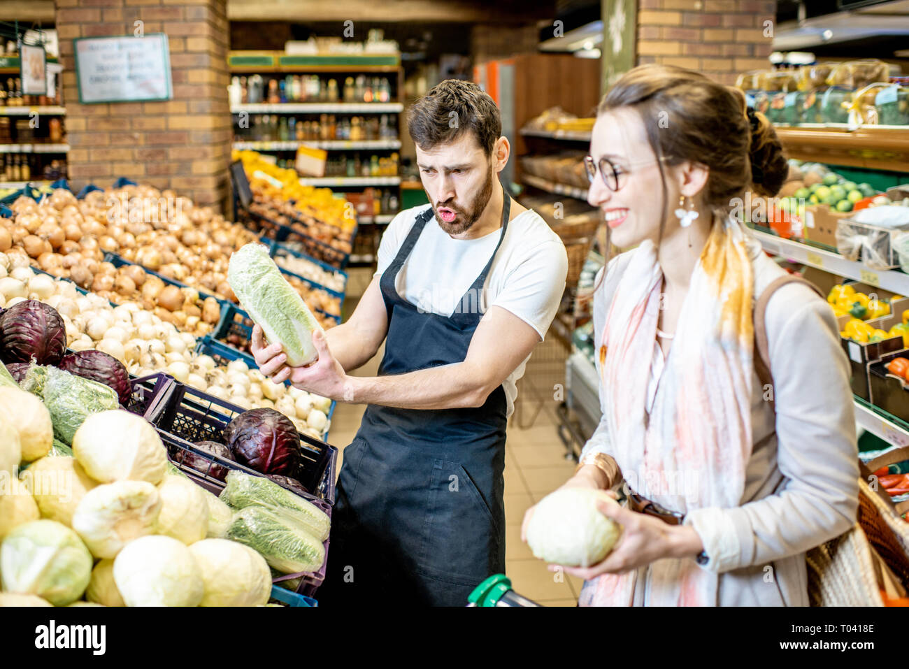 Shop worker helping young woman client to chooose vegetables in the ...