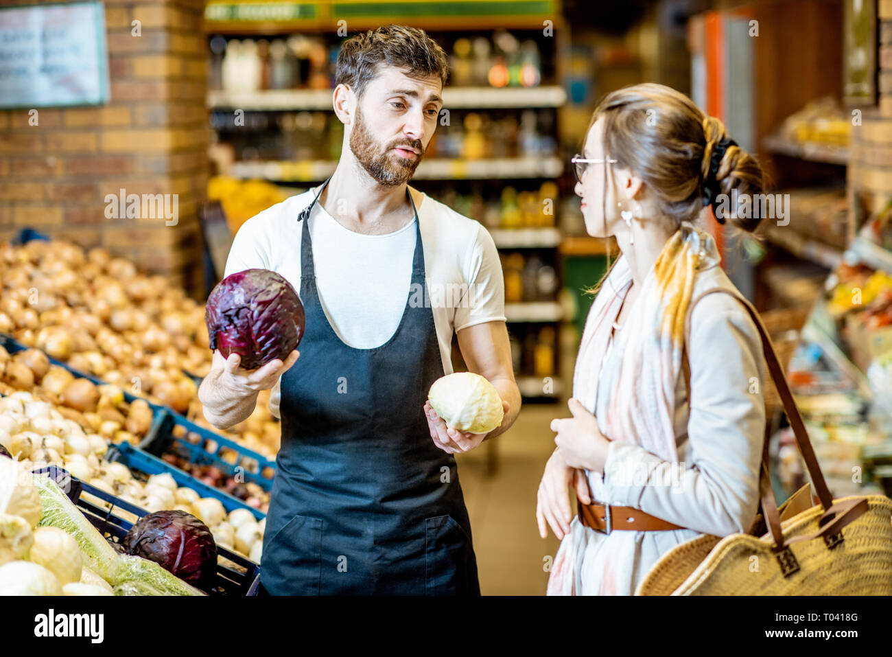 Shop worker helping young woman client to chooose vegetables in the ...