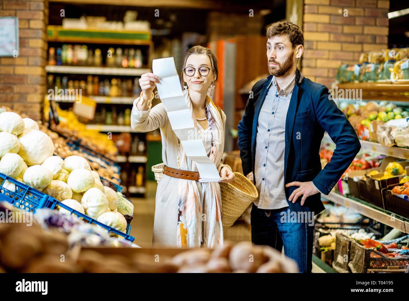 Young couple buying food standing together with long shopping list in ...