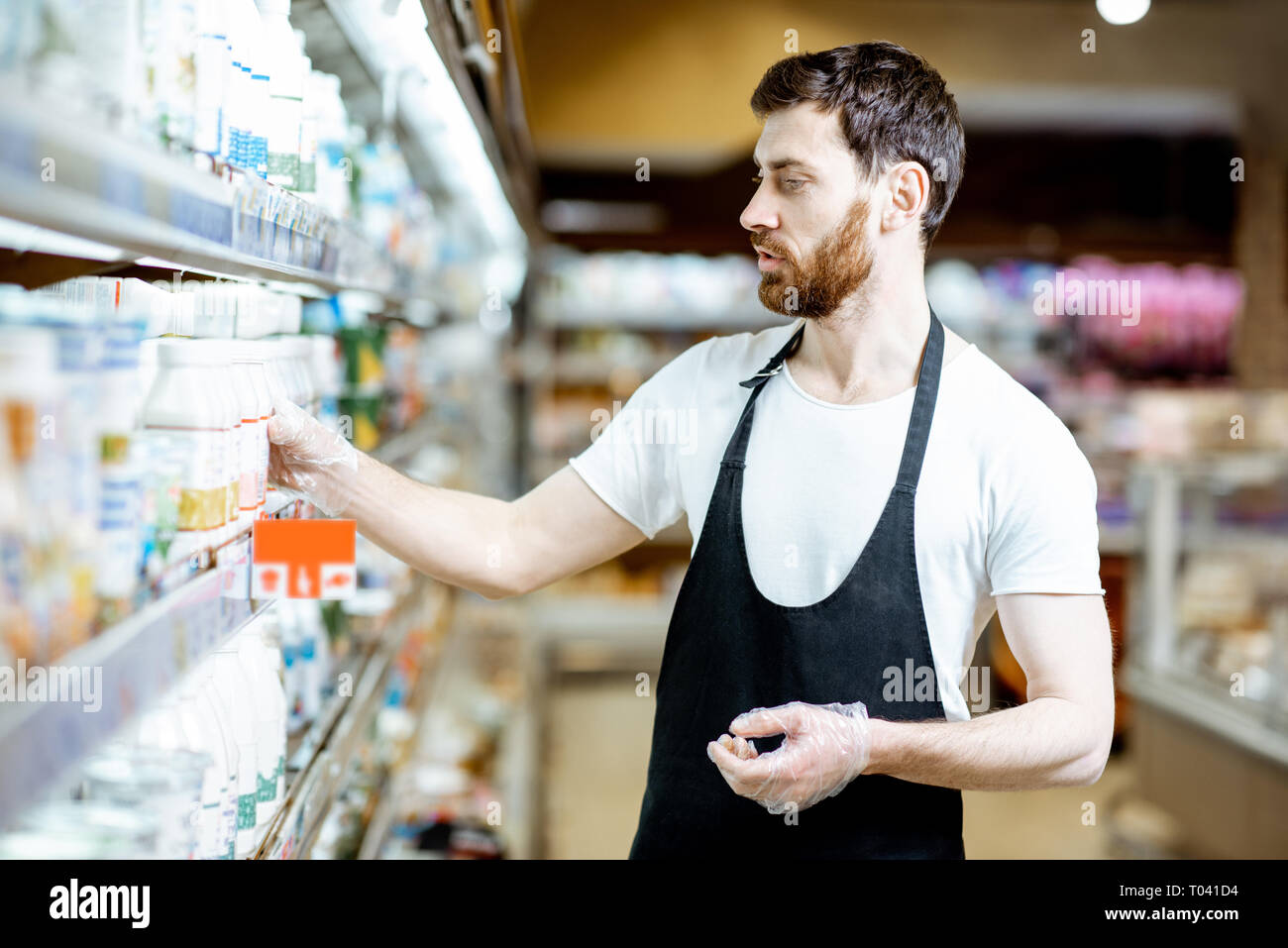 Shop worker looking on the bottles with milk standing near the shelves ...