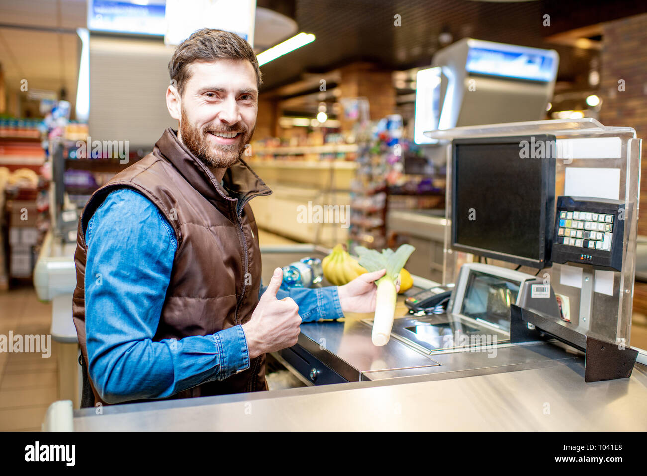 Portrait of a happy and cheerful man as a cashier, sitting at the cash ...
