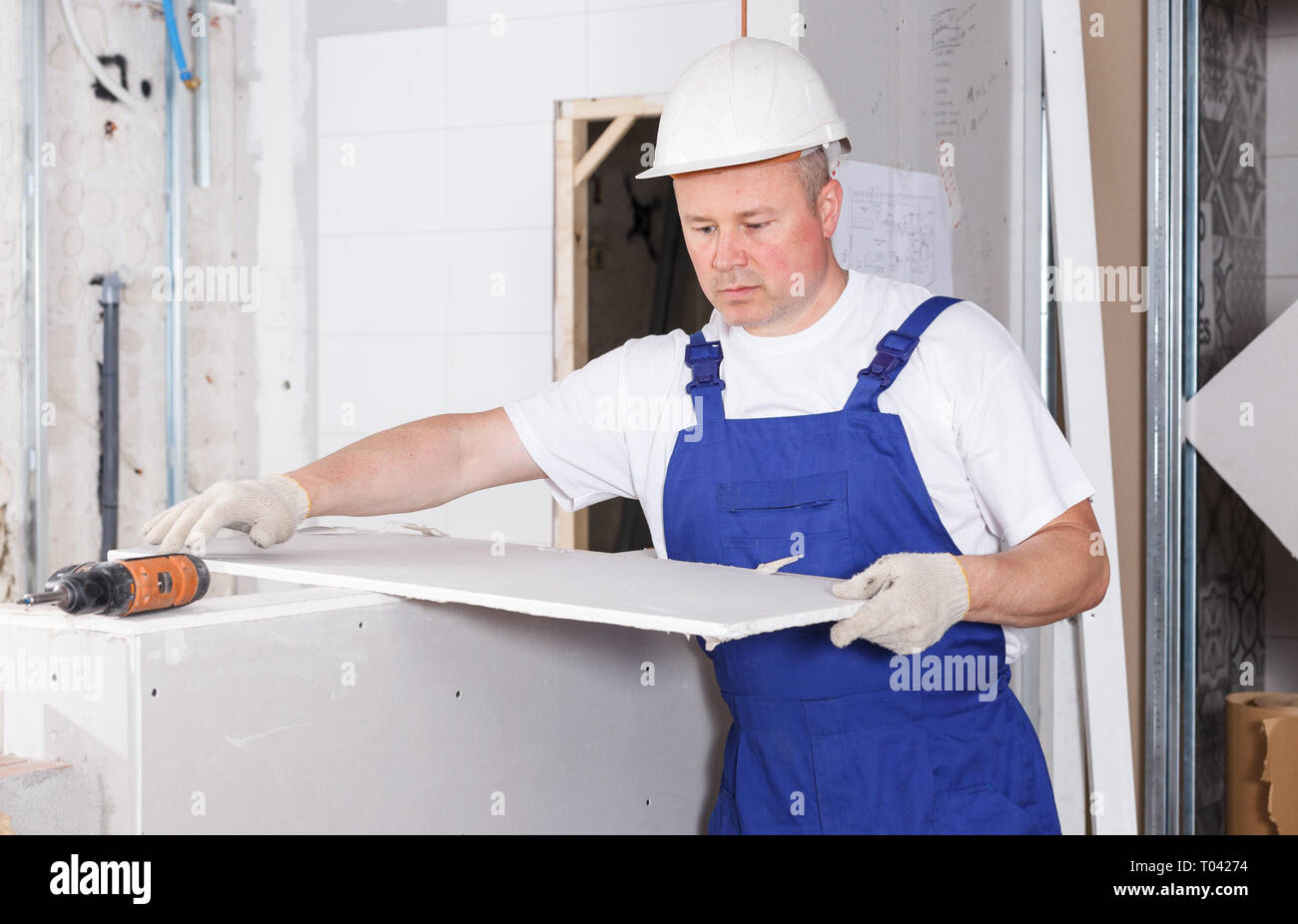 Construction worker engaged in drywall mounting in overhauls indoors ...