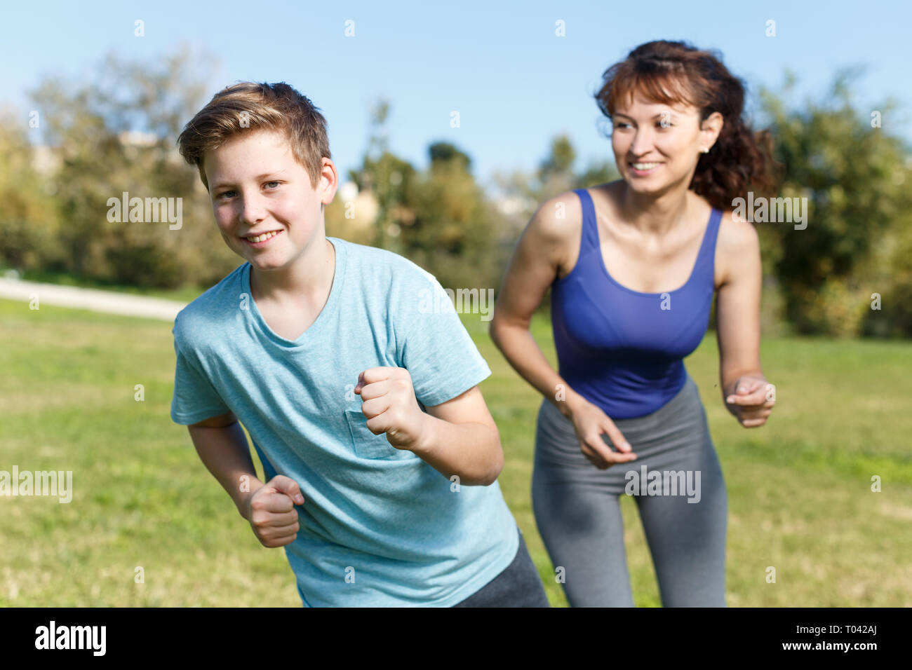 Portrait of young athletic woman and tween boy running outdoors at ...