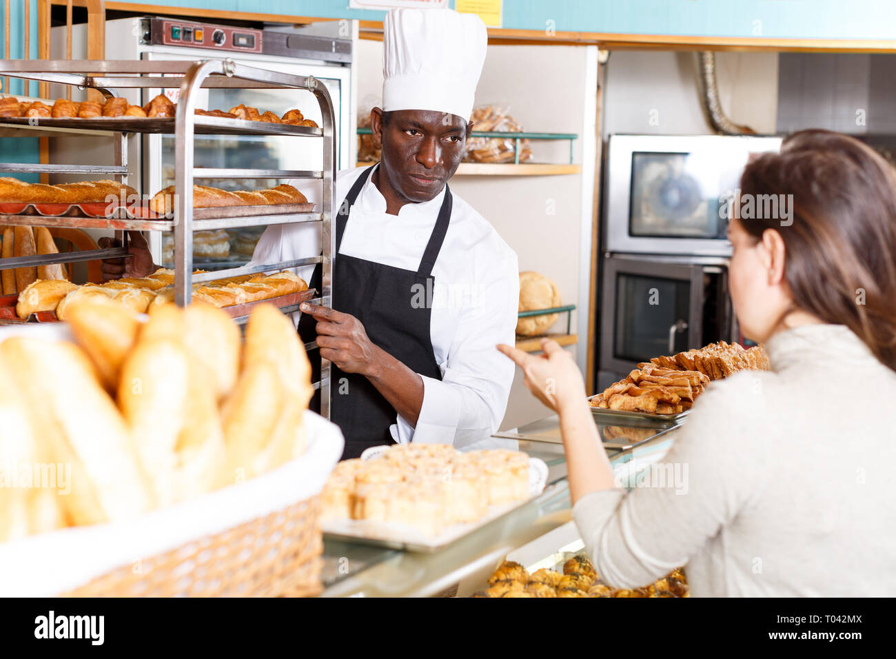 Polite male baker working behind counter in store of his bakery ...