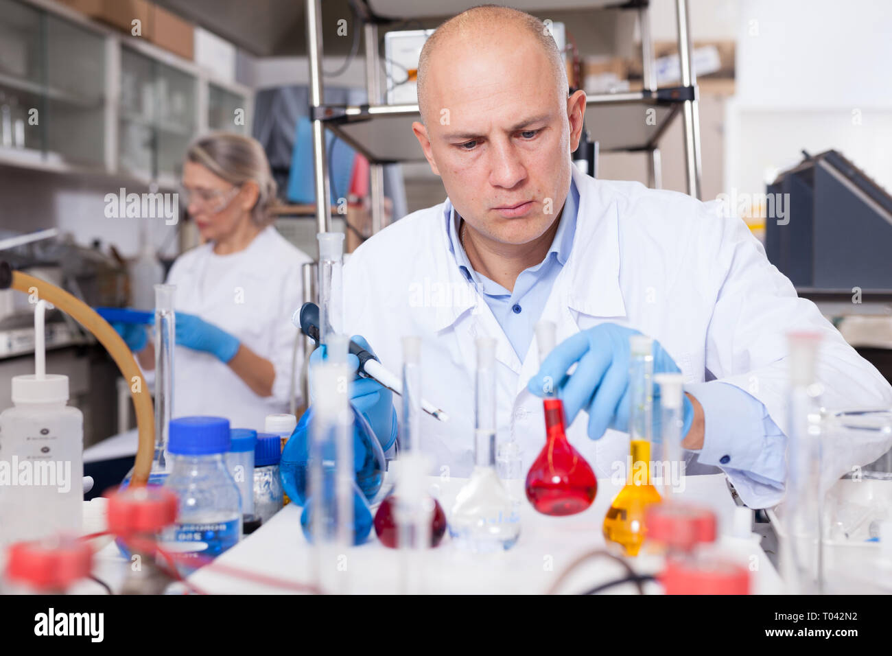 Focused lab technician working with reagents in test tubes during ...