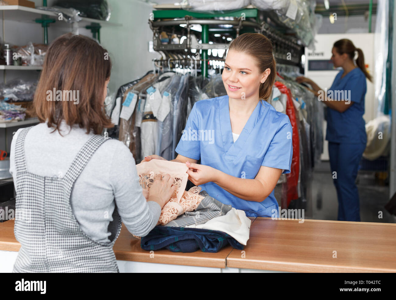 Female worker of dry cleaner checking clothes of customer on reception ...