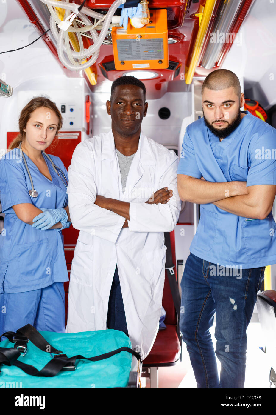 Three positive smiling efficient ambulance doctors posing in ambulance ...