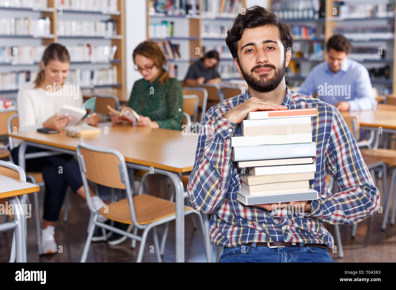 positive student sitting with pile of books in university library on ...