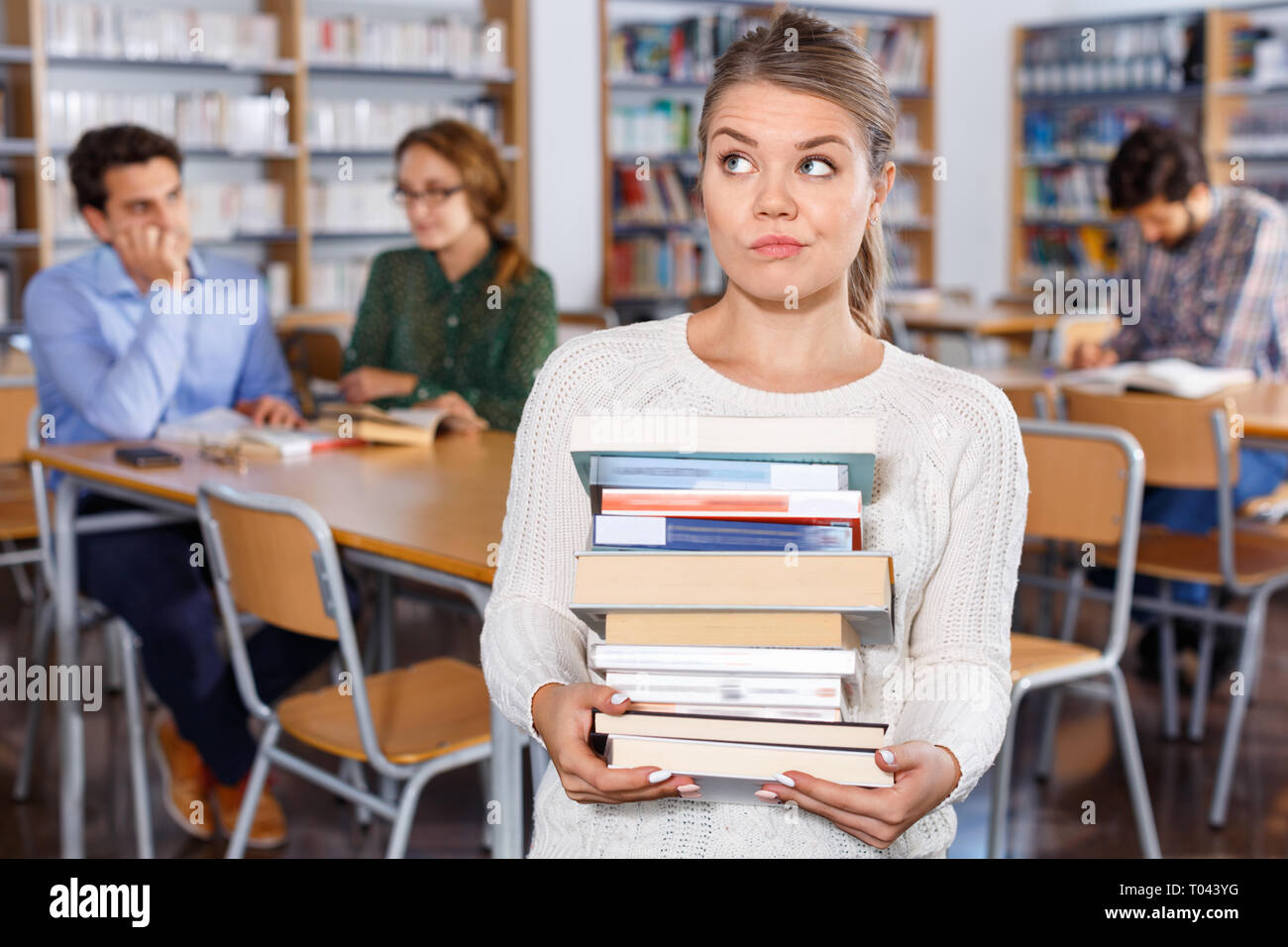 Annoyed angry young charming girl sitting with pile of books in high ...
