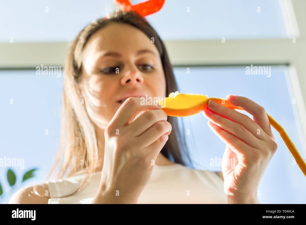 Young happy beautiful woman eating orange slice at home near the window ...