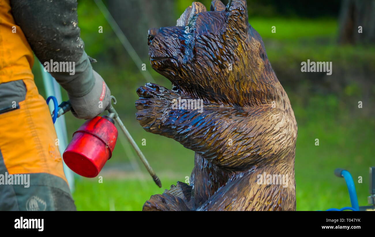 A man spraying a paint on a dog wood scultpure it is a big dog that is ...