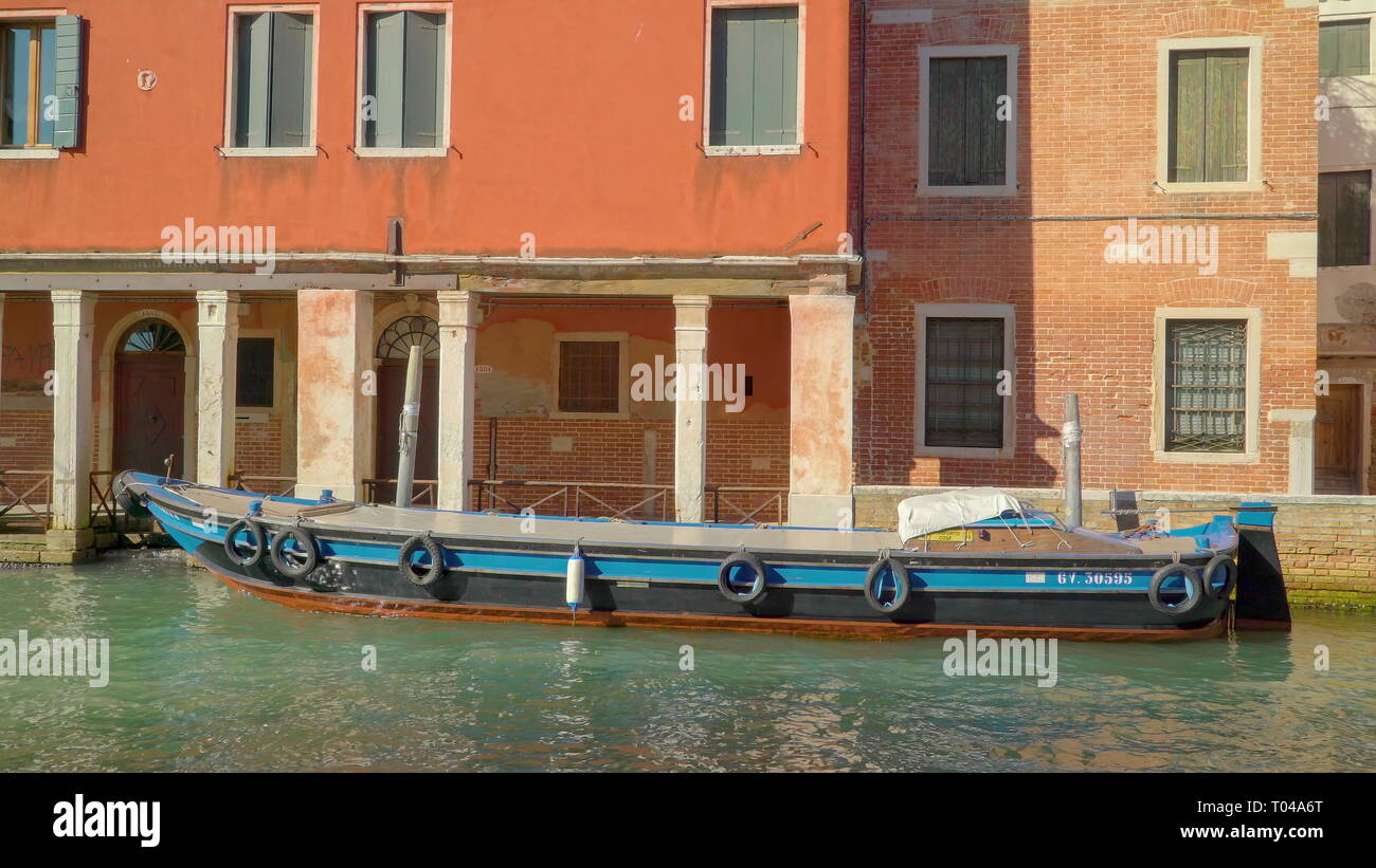The big blue boat docking on the side of the canal with the small black ...