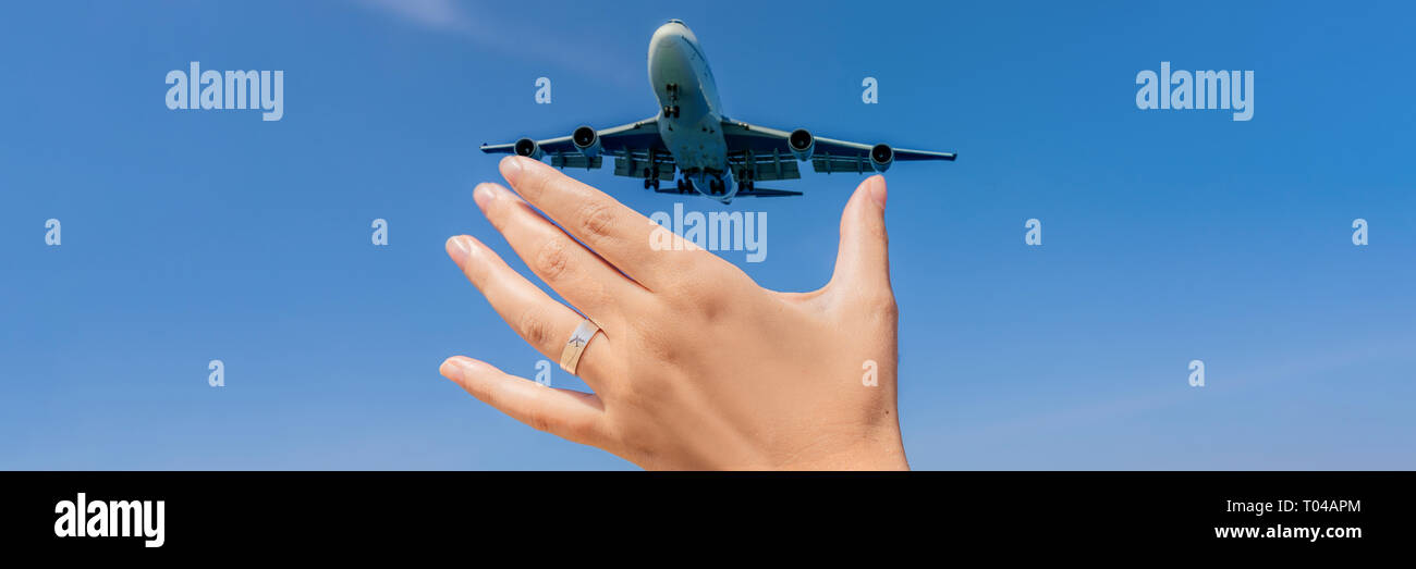 Female hand with a ring with a drawn plane holding a plane flying in ...