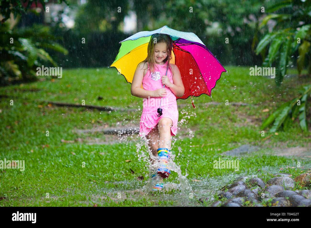 Kid playing out in the rain. Children with umbrella and rain boots play ...