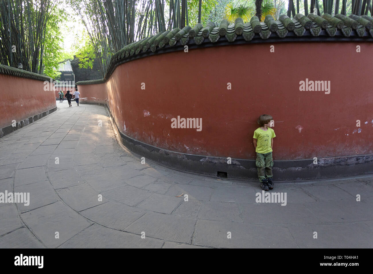 Boy walking between curvy red walls passage surrounded by bamboo forest ...