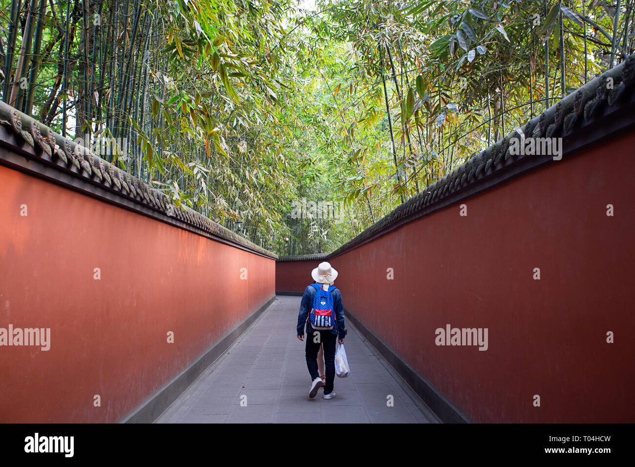 Couple walking at curvy red walls passage surrounded by bamboo forest ...