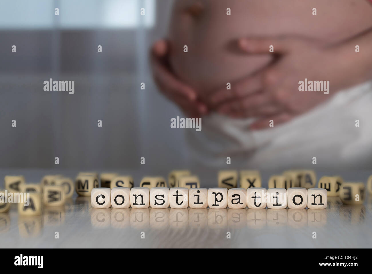 Word CONSTIPATION composed of wooden letters. Pregnant woman in the ...