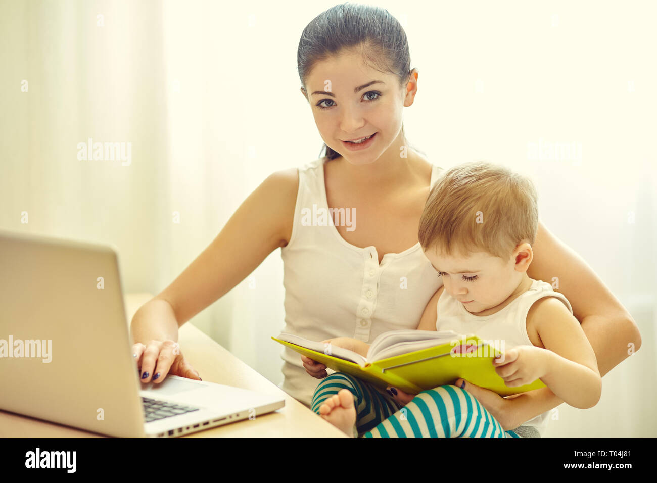 Mother with child works at the computer at home and reading a book ...