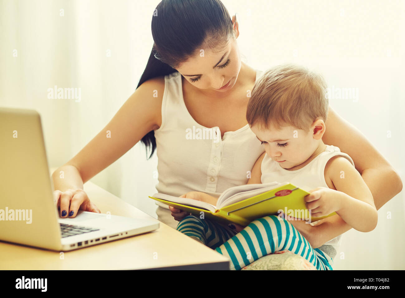 Mother with child works at the computer at home and reading a book ...