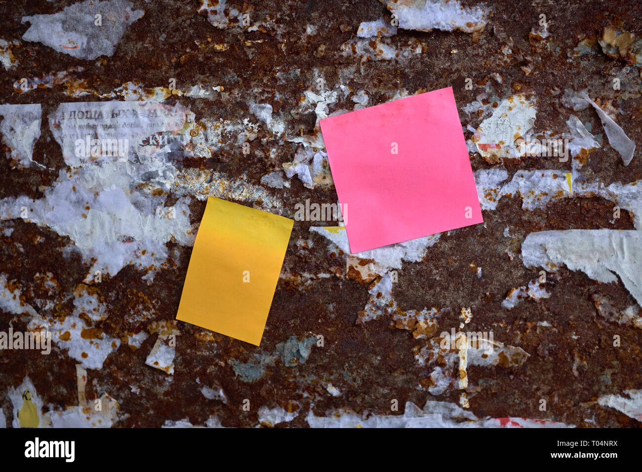 Two blank color paper on torn posters on rusted steel wall. A lot of ...