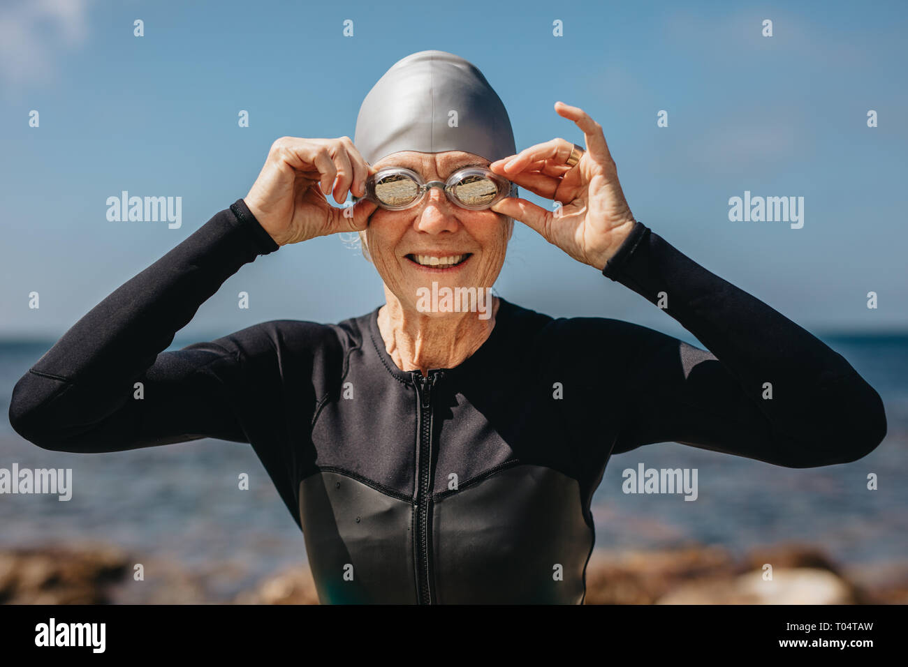 Portrait of a smiling senior female swimmer with sea in the background ...