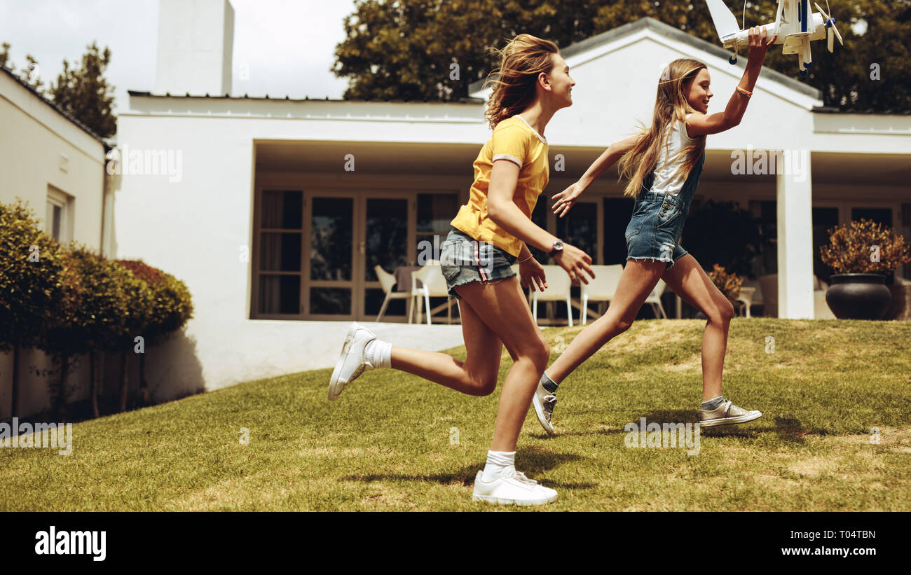 Two girls running on grass in backyard flying a toy plane. Girls having ...
